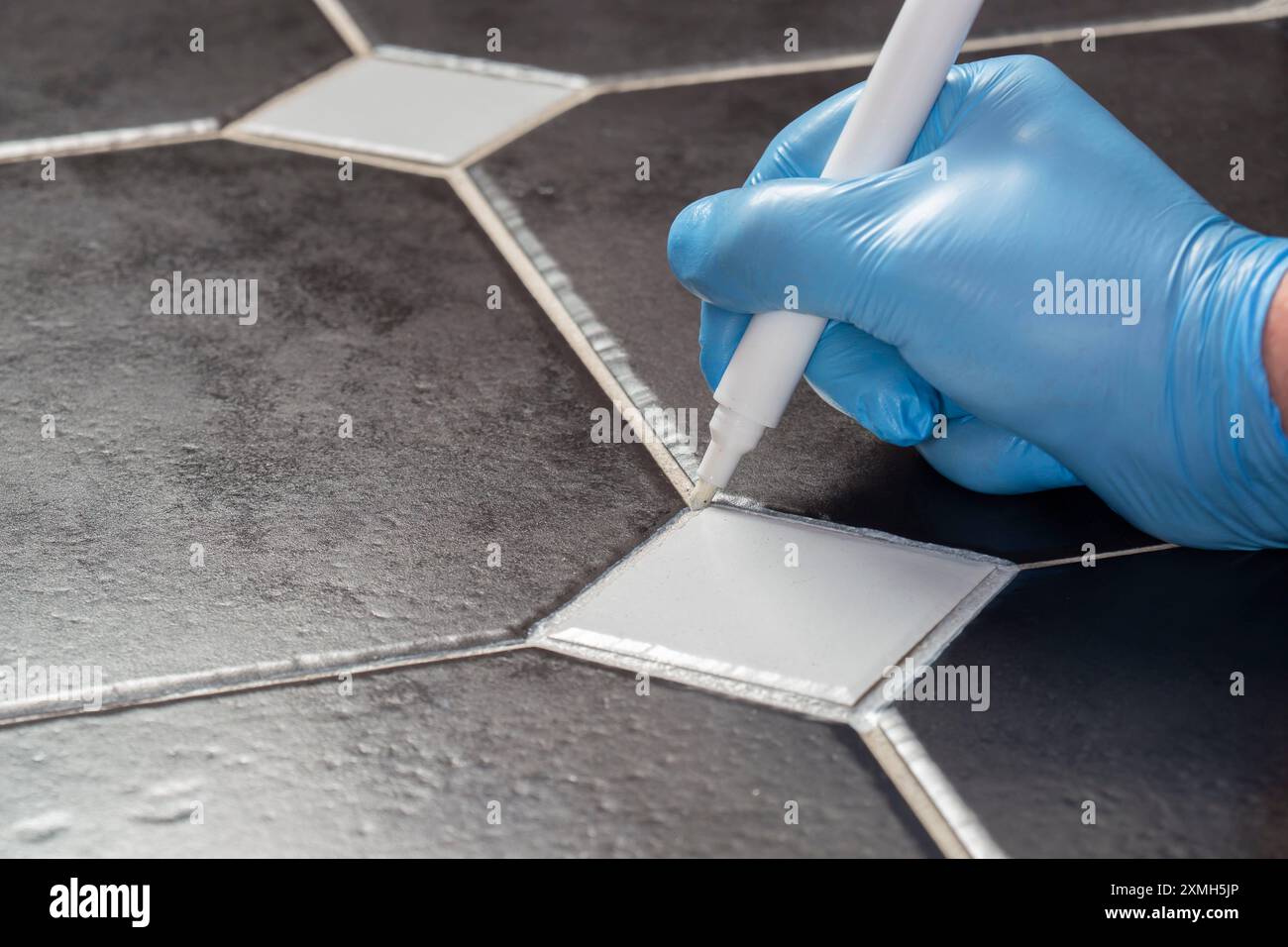 Person wearing gloves using grout pen on floor tiles to restore white ...