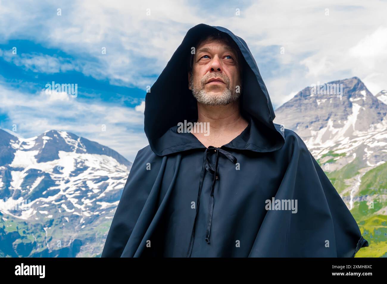 Mysterious elderly male monk wearing a hooded cloak, standing amidst ...