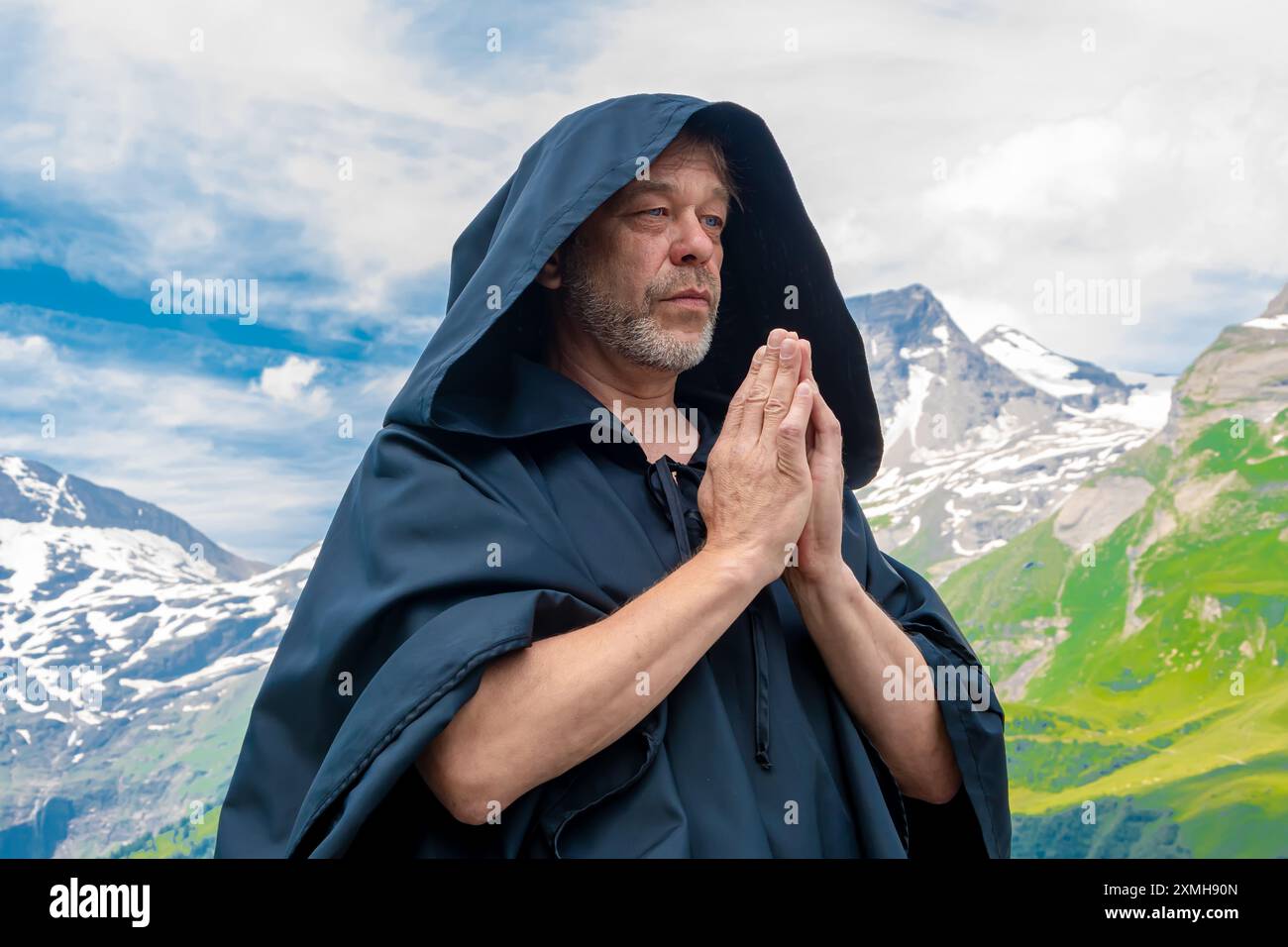 Mysterious elderly male monk wearing a hooded cloak, standing amidst ...