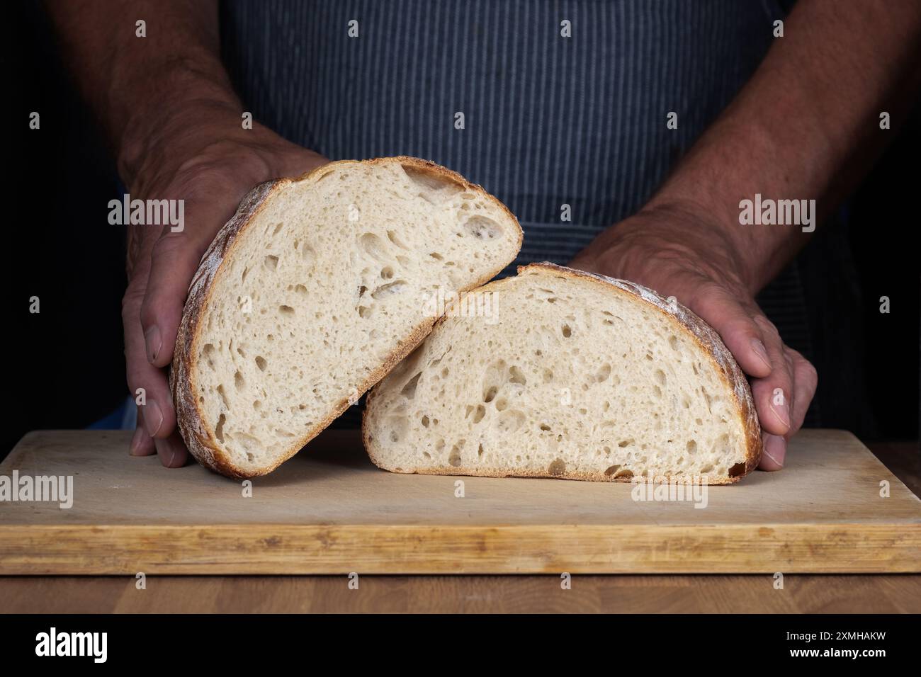 UK. A baker holds two halves of a freshly baked homemade sourdough loaf ...