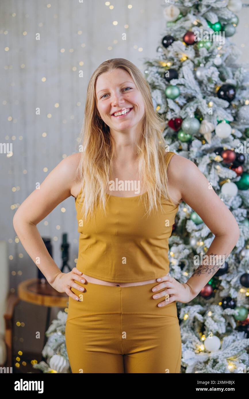 Cheerful woman in mustard activewear stands in front of a decorated ...