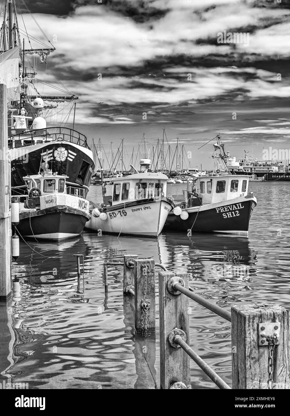 Three small fishing boats are moored together with larger boats behind ...
