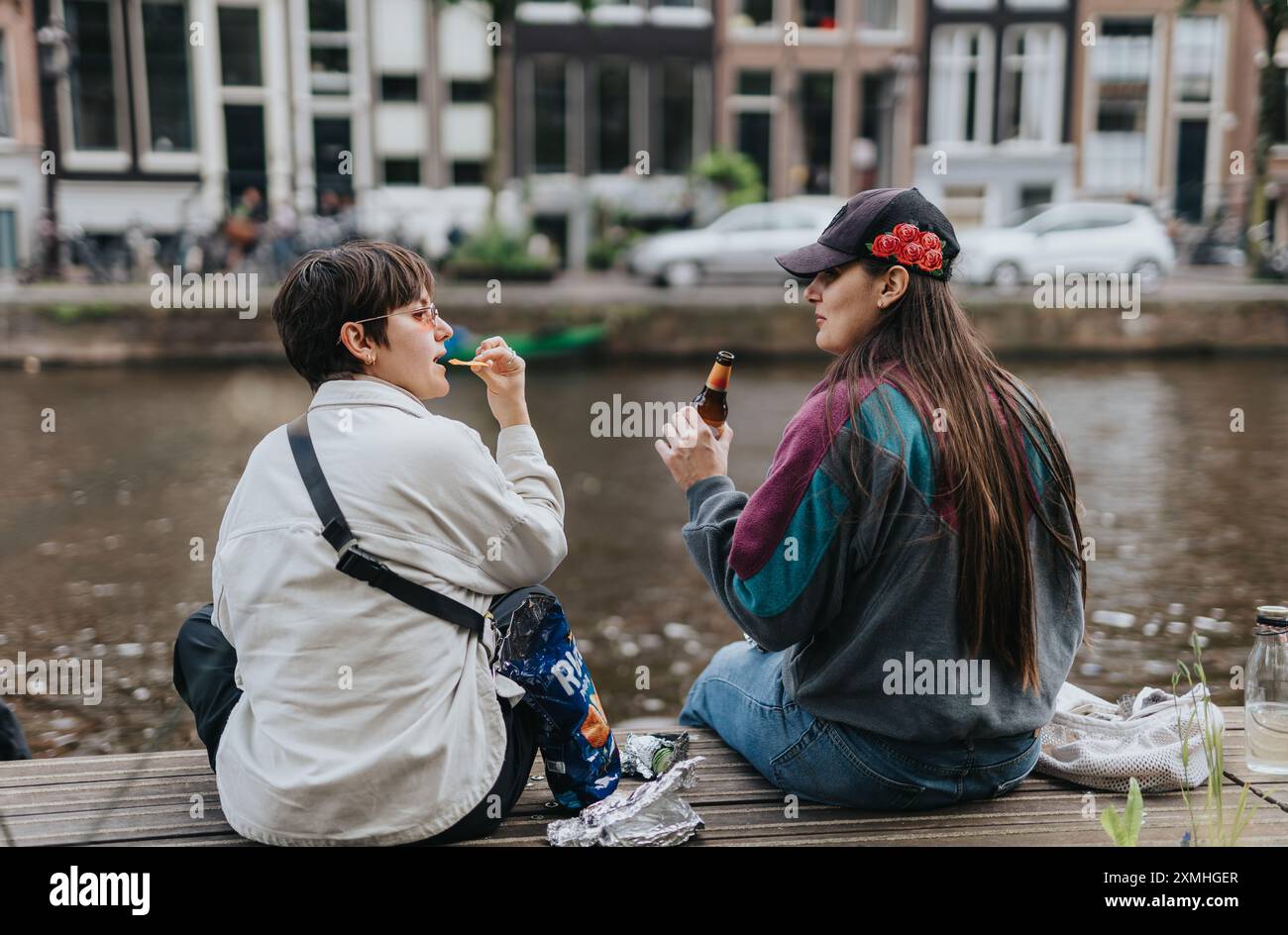 Two friends relaxing by an Amsterdam canal, enjoying drinks and snacks ...