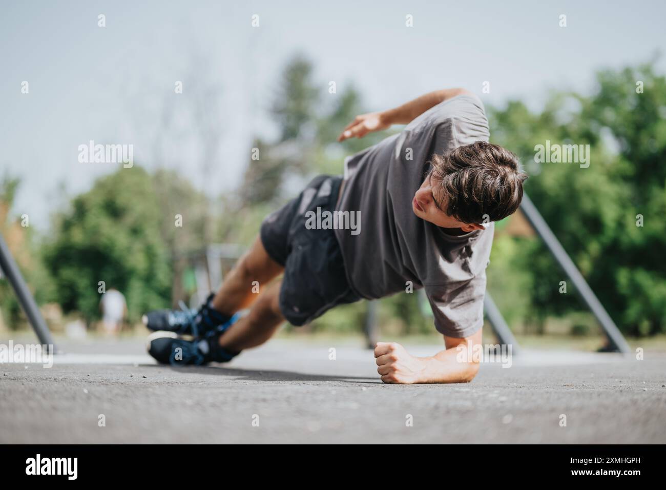 Young man performing side plank exercise outdoors in a park setting ...