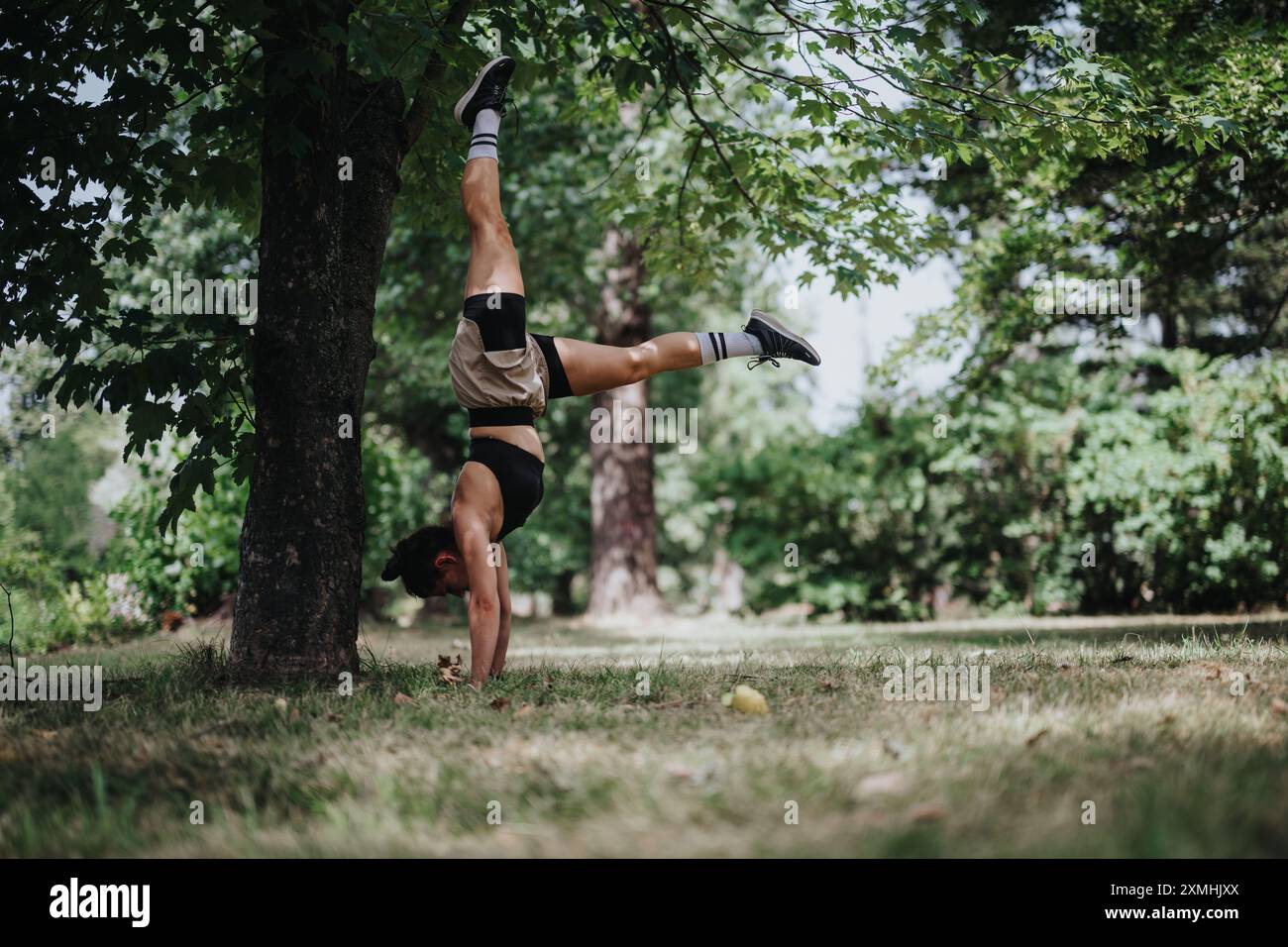 Woman performing handstand push-up against tree in outdoor park setting ...