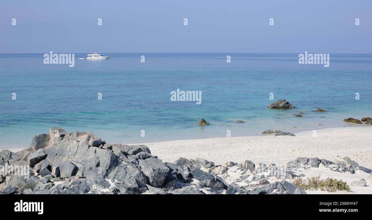White sand and rocky beach with a boat in turquoise waters on Masirah ...
