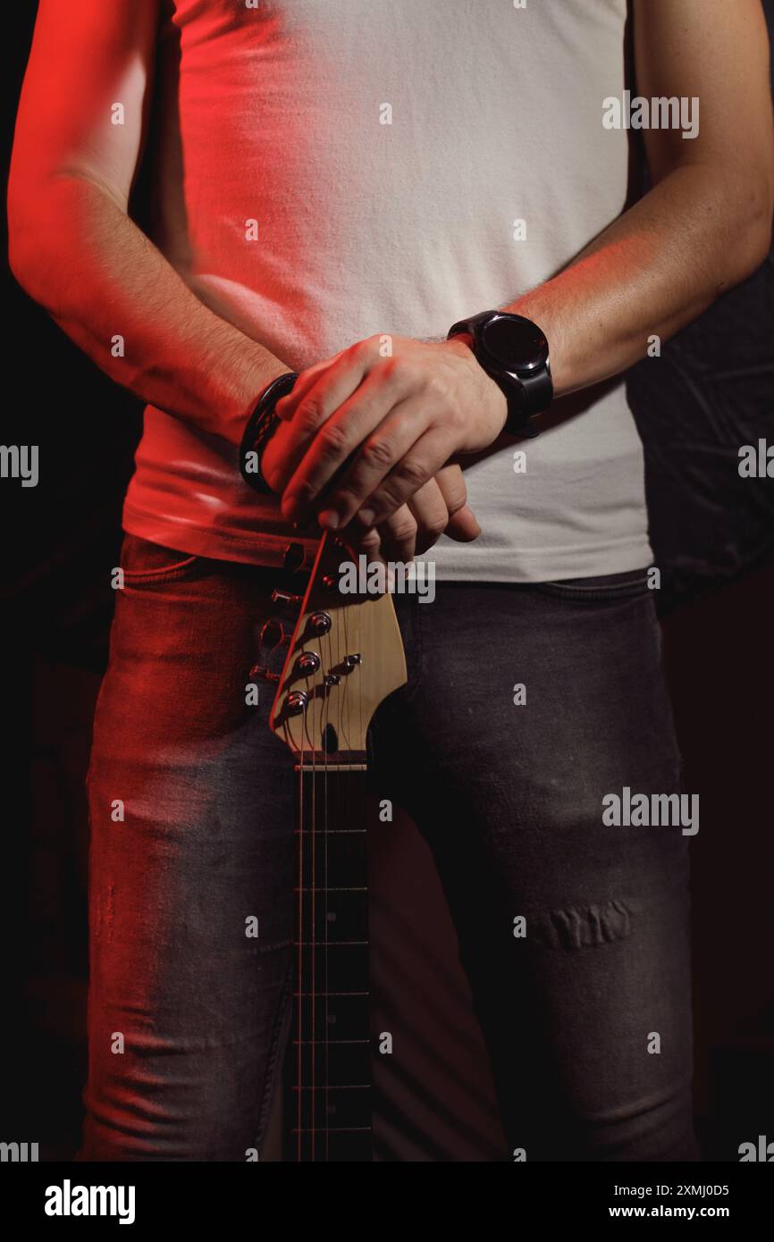 A guitarist illuminated with red light, holding the neck of an electric ...