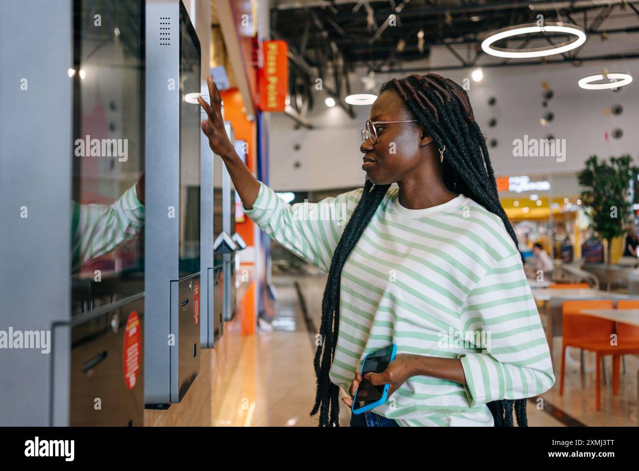 Black Woman with glasses and striped shirt using a touch screen kiosk ...