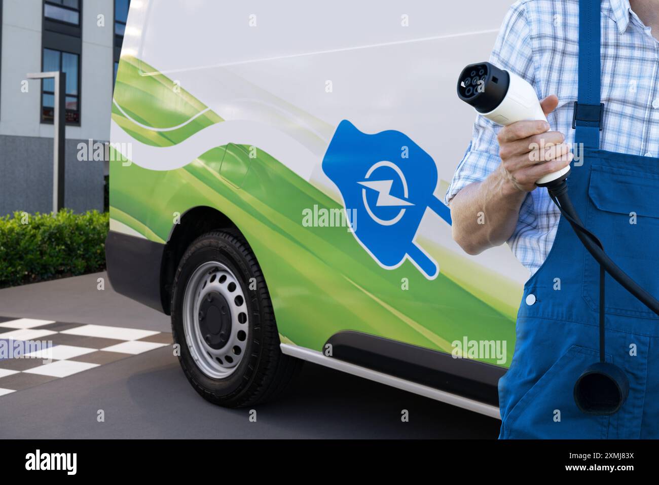Man holds electric vehicle charging plug. Electric van in the ...