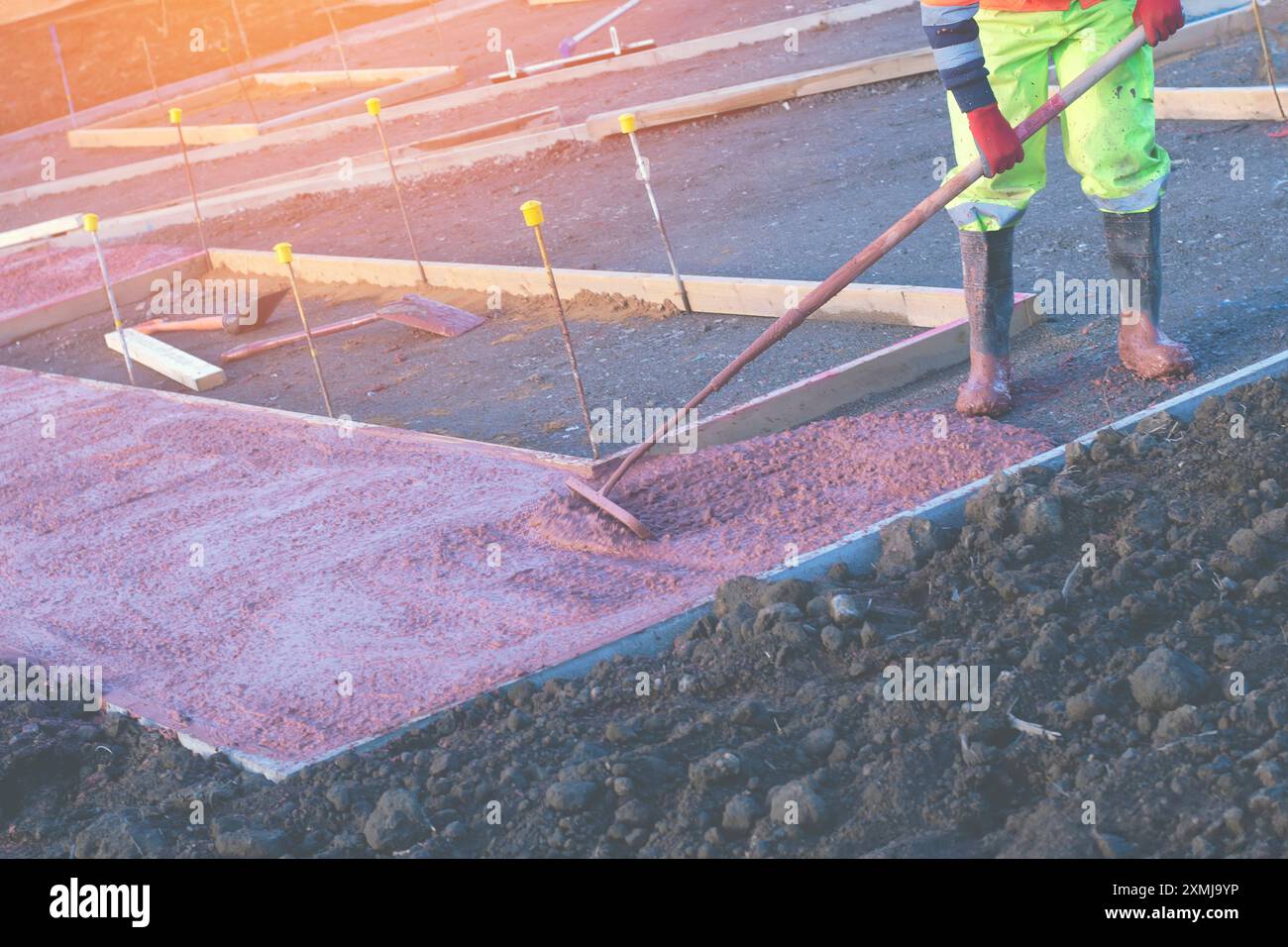 Builders pouring and levelling wet ready-mix concrete into formwork ...