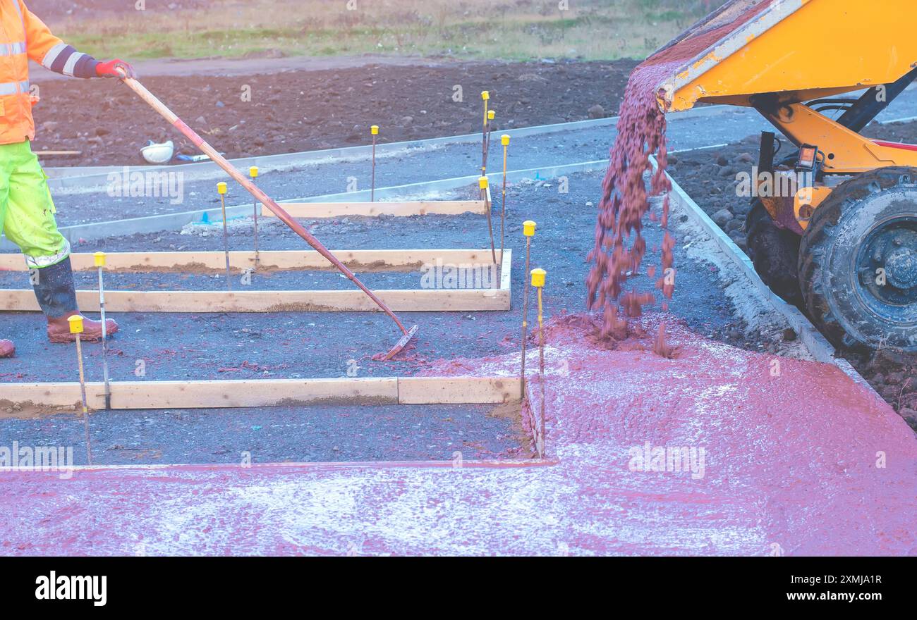 Builders pouring and levelling wet ready-mix concrete into formwork ...