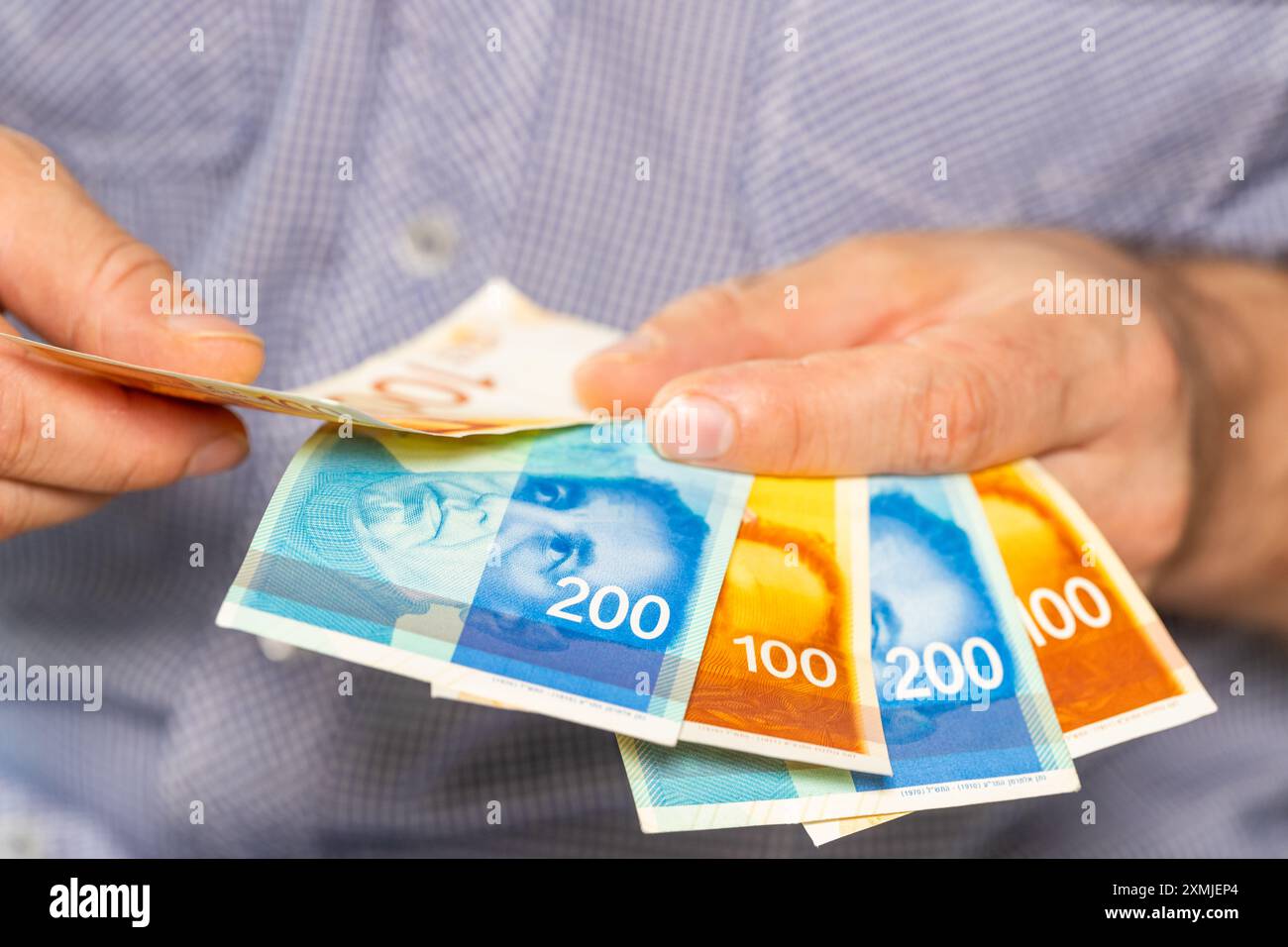 A man holds a stack of Israeli money in his hand and takes out a 100 ...