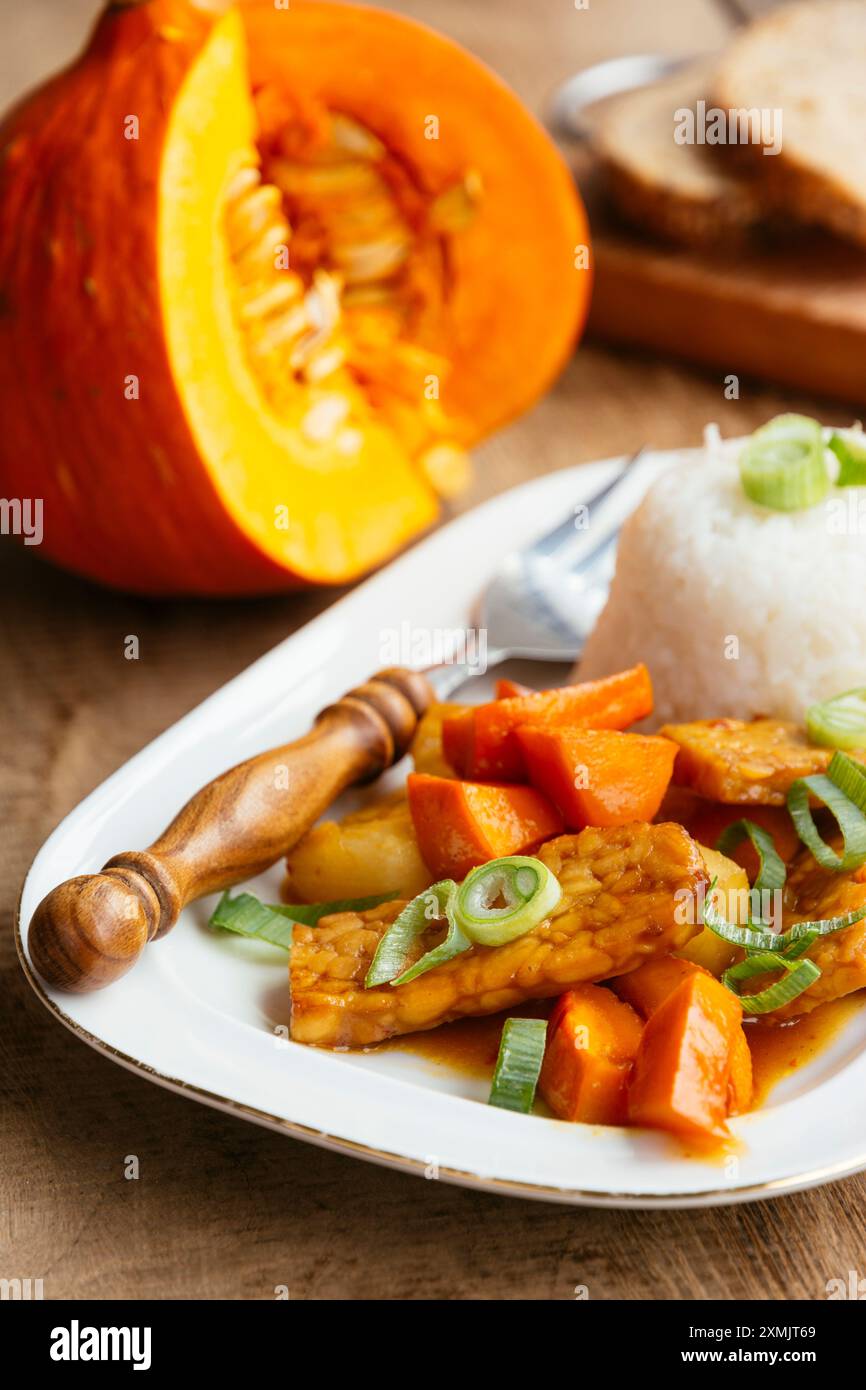 Sweet-sour tempeh with red uchi kuri squash and rice on a plate Stock ...