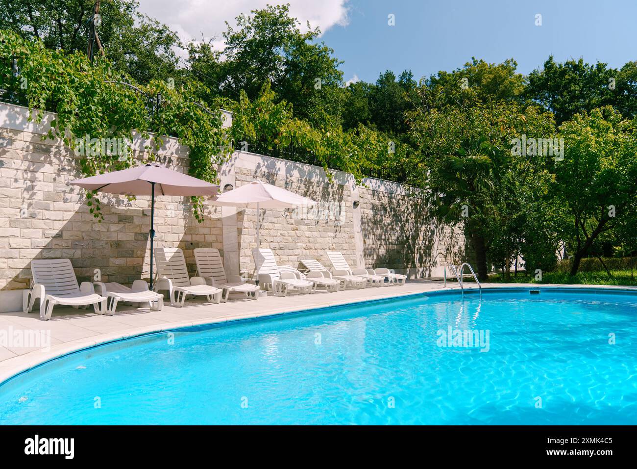Swimming pool among green trees in the courtyard near a brick fence ...