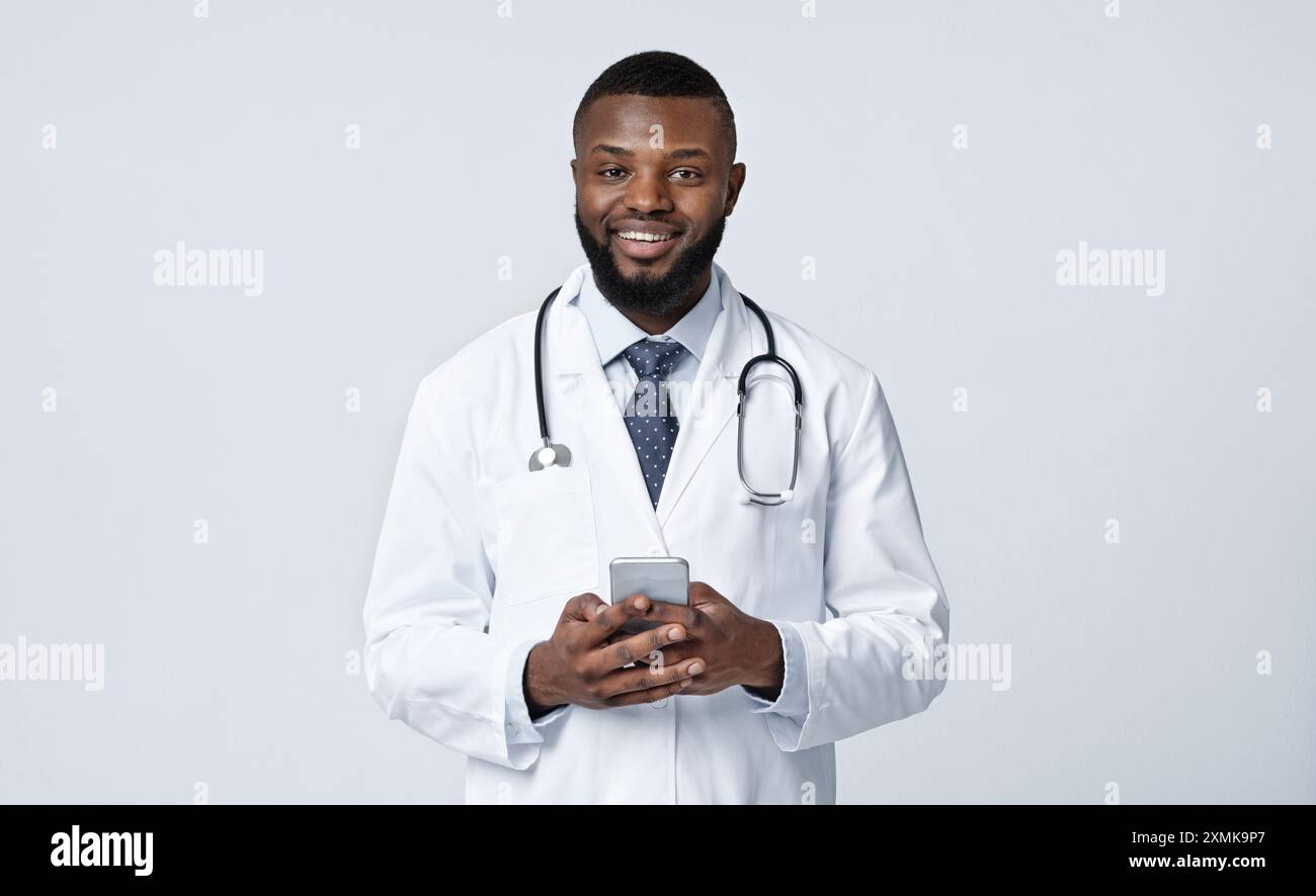 Happy african doctor holding mobile phone, white background Stock Photo ...
