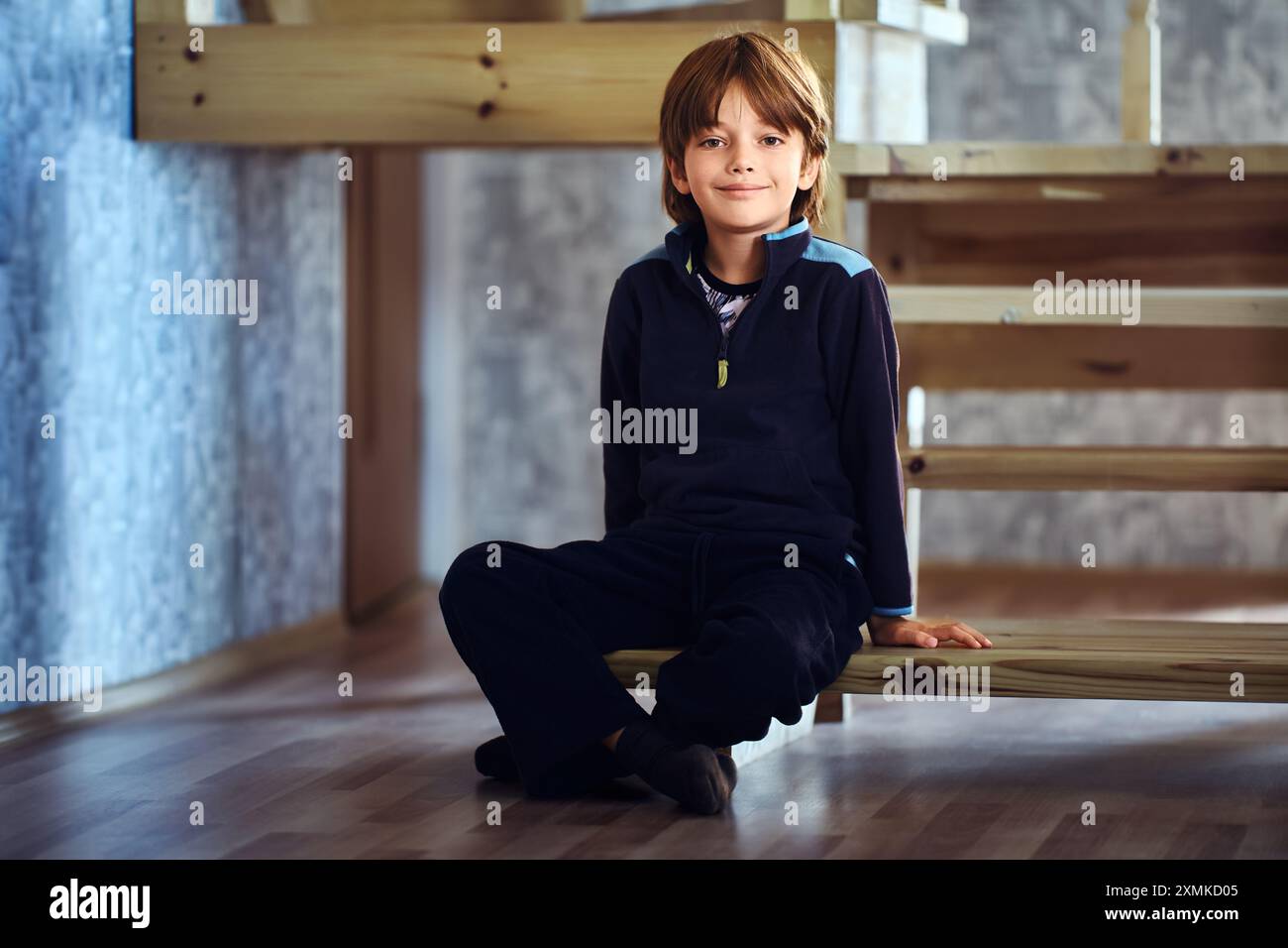 Satisfied European boy of seven years old is sitting on step of stairs ...