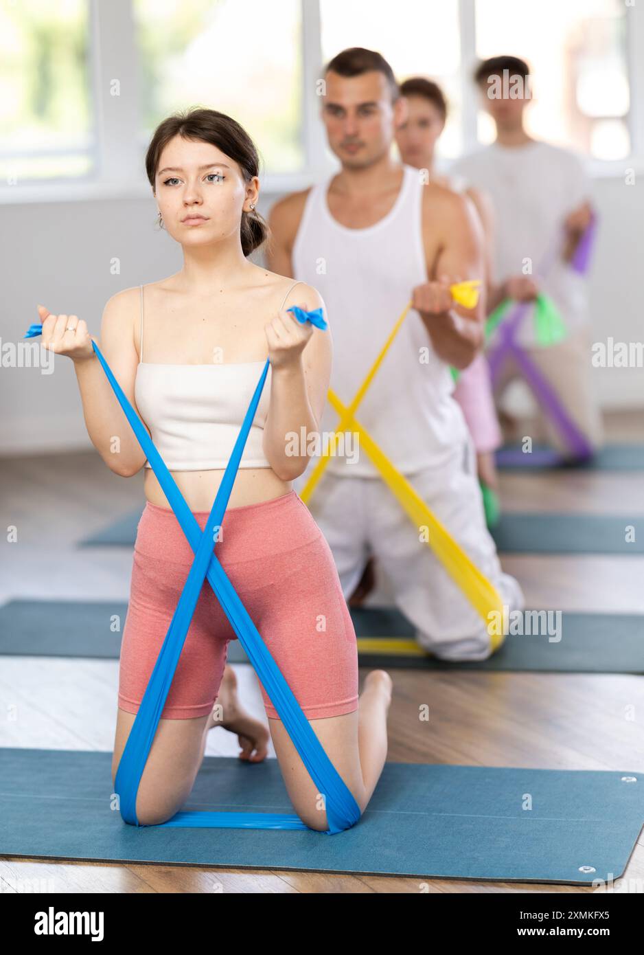 Young girl doing arm workout with resistance band standing on knees ...