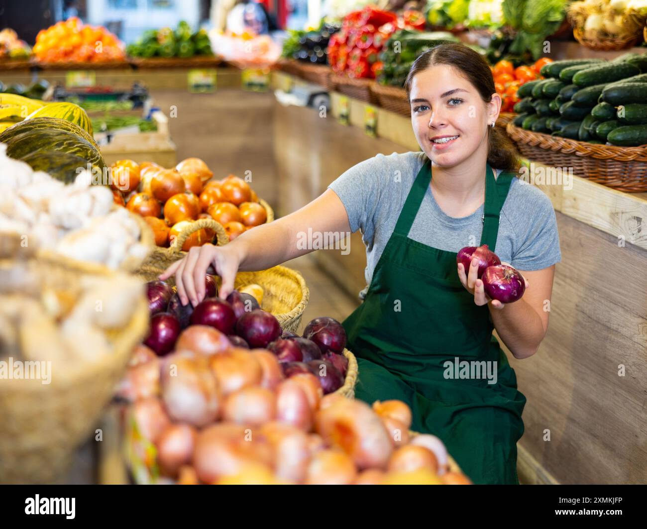 Female grocery store worker arranges red onion and other vegetables on ...
