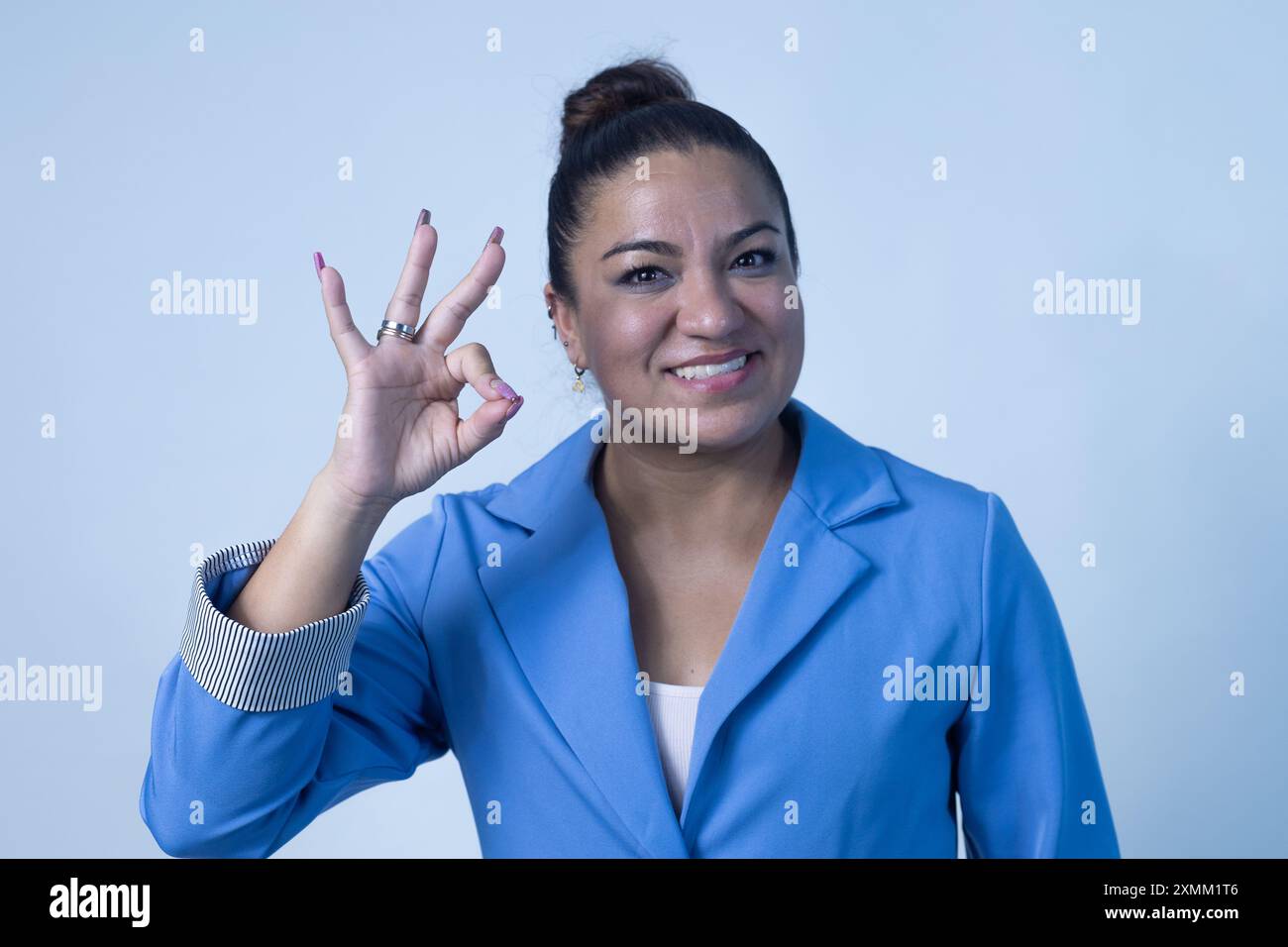 A confident woman in a stylish blue business suit smiles, making an OK ...