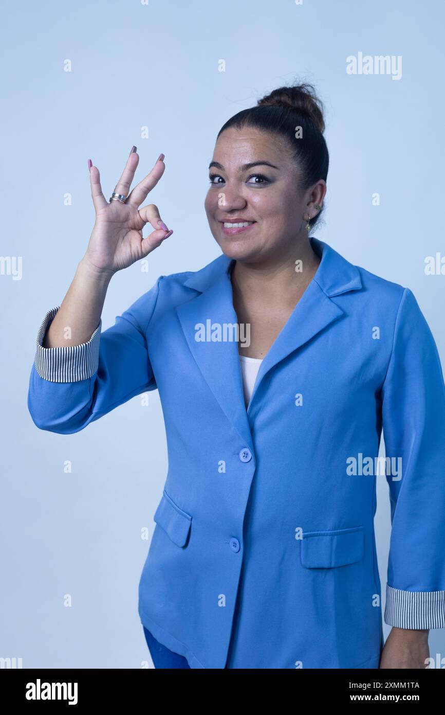 A woman wearing a blue blazer smiles brightly and makes an okay hand ...