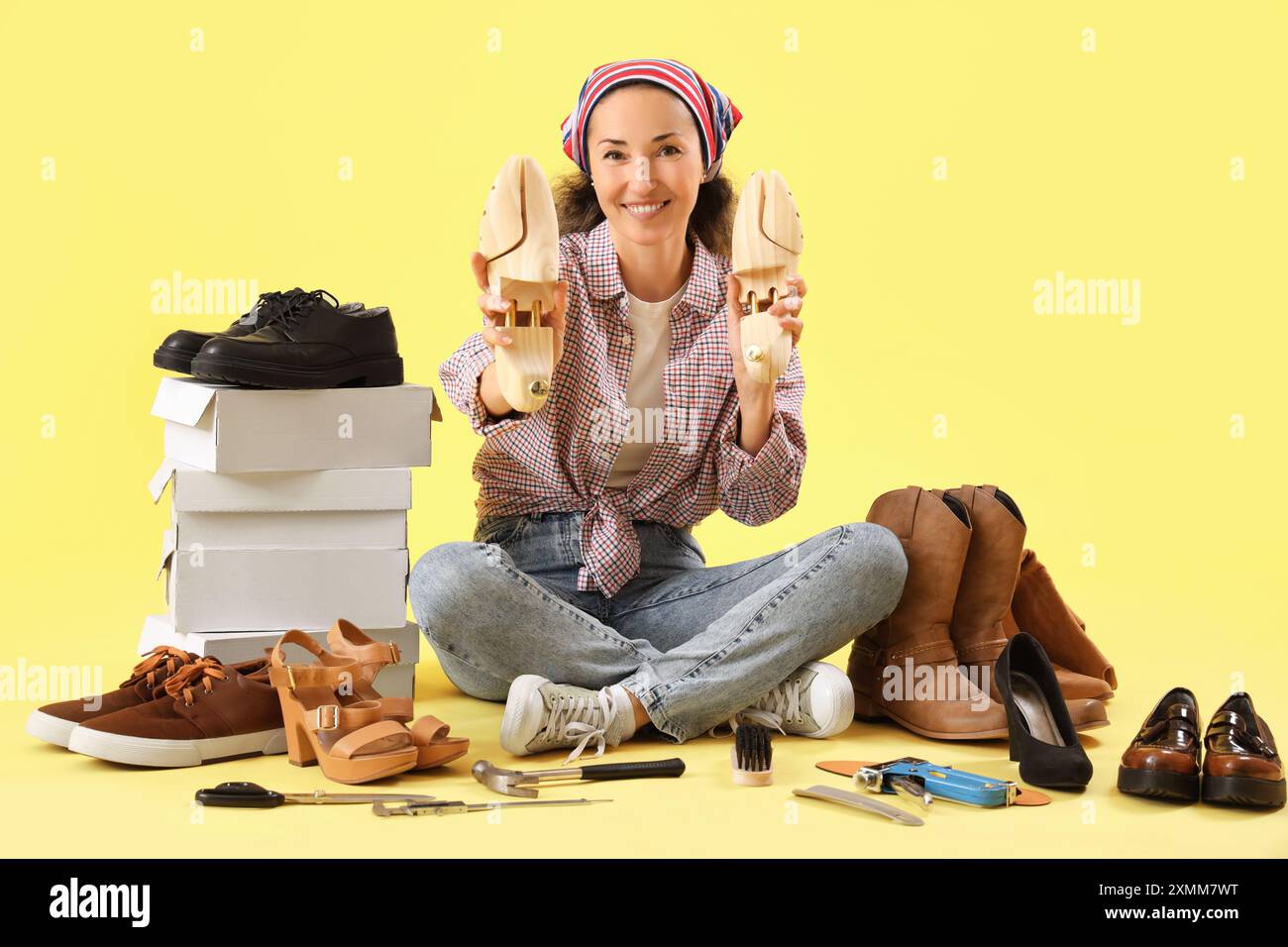 Female shoemaker with wooden shoe trees sitting on yellow background ...