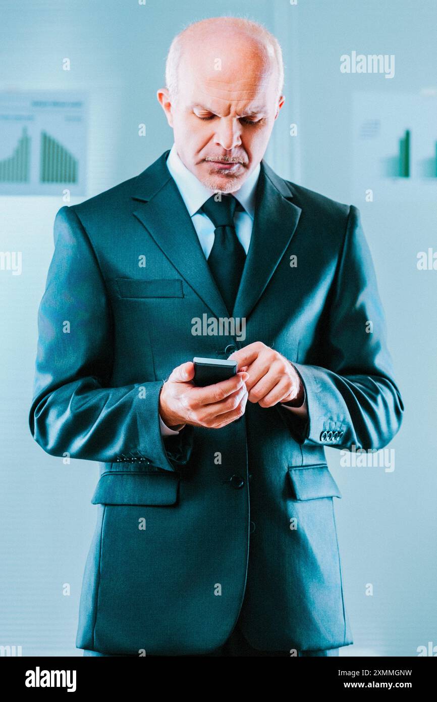 Mature businessman in a sharp suit uses his smartphone in an office ...