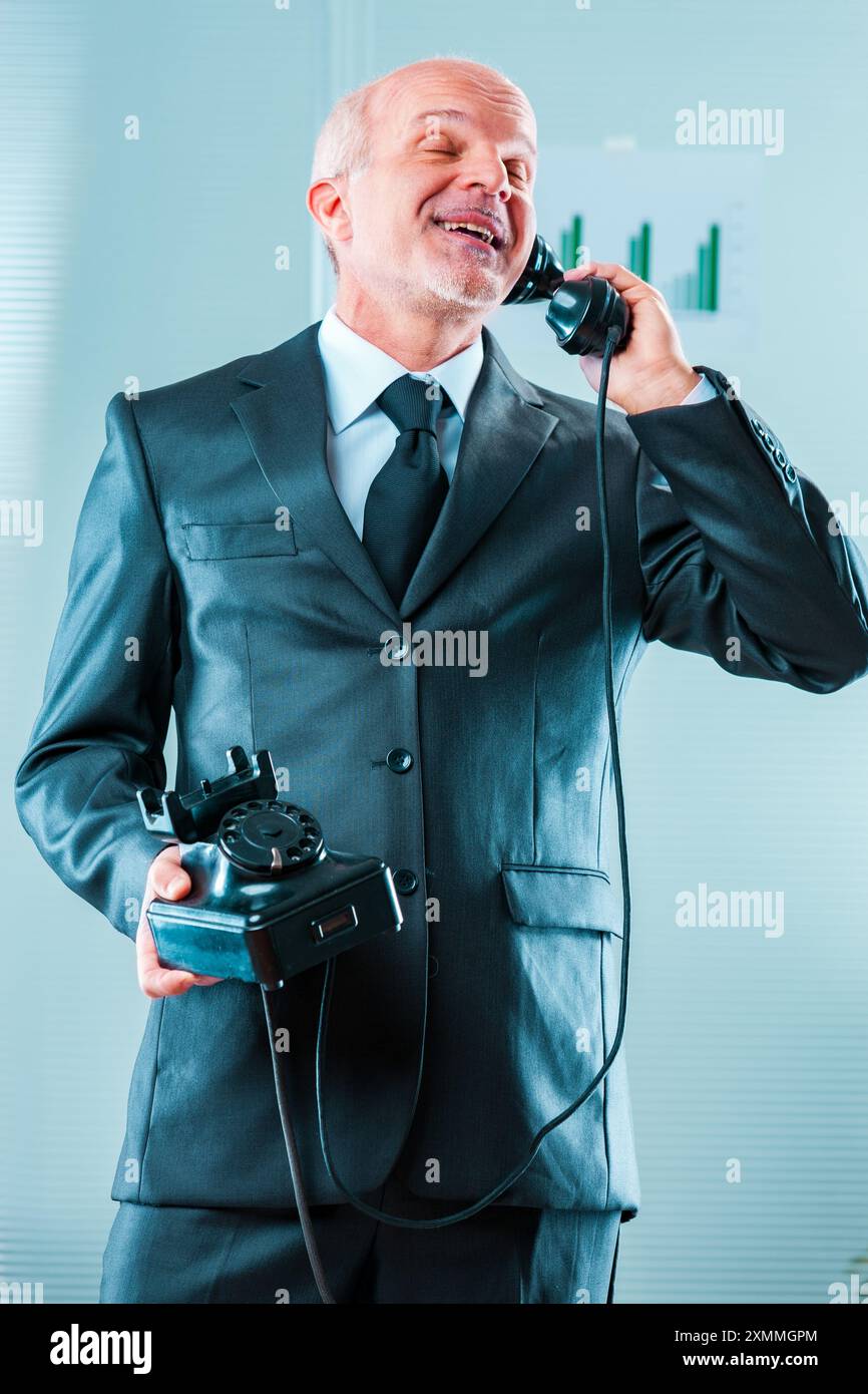 Proud businessman in a dark suit smiles while holding a classic rotary ...