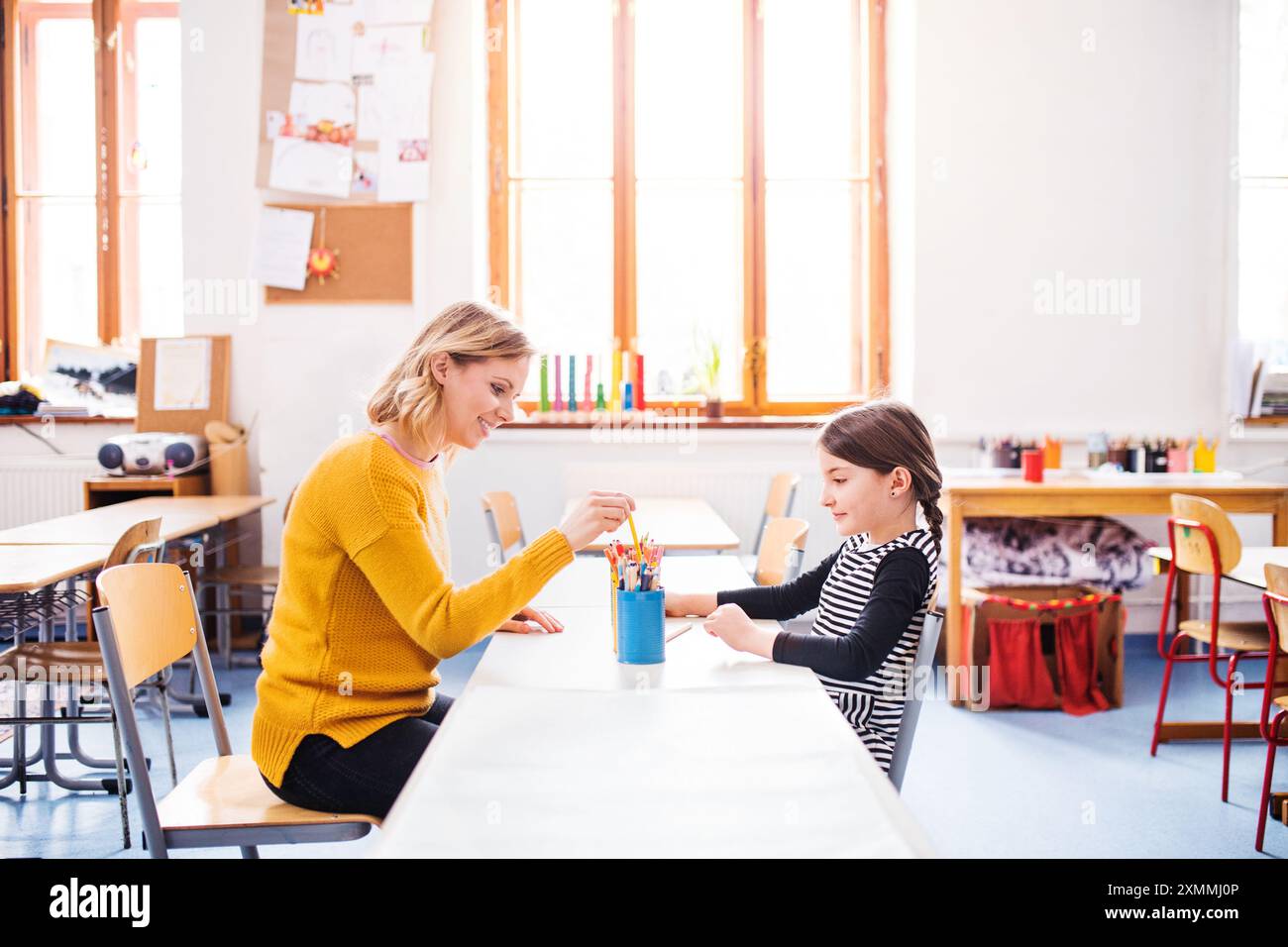 Hardworking teacher learning with young schoolgirl in classroom ...
