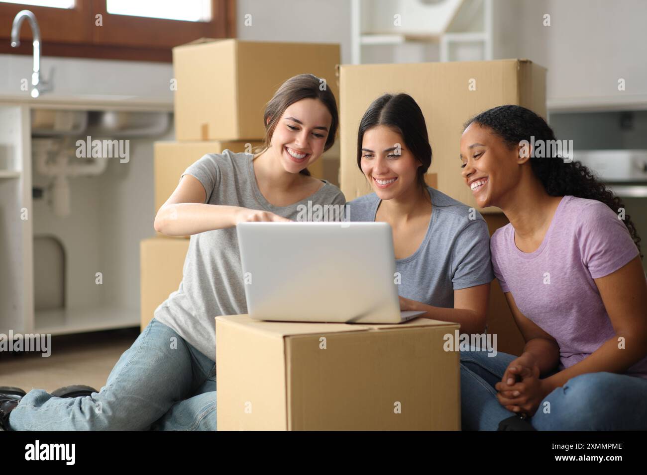 Three happy multi ethnic roommates checking laptop moving house Stock ...