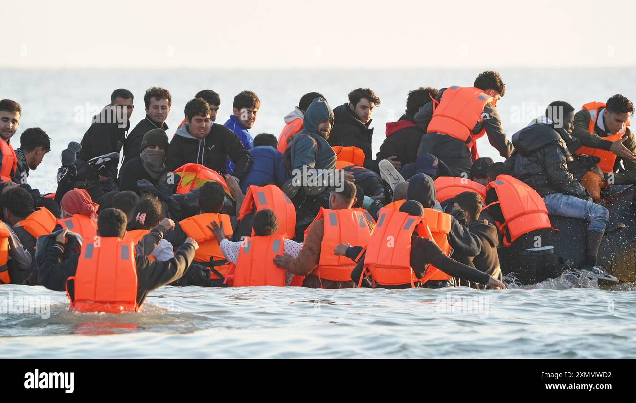 A group of people thought to be migrants wade through the sea to ...
