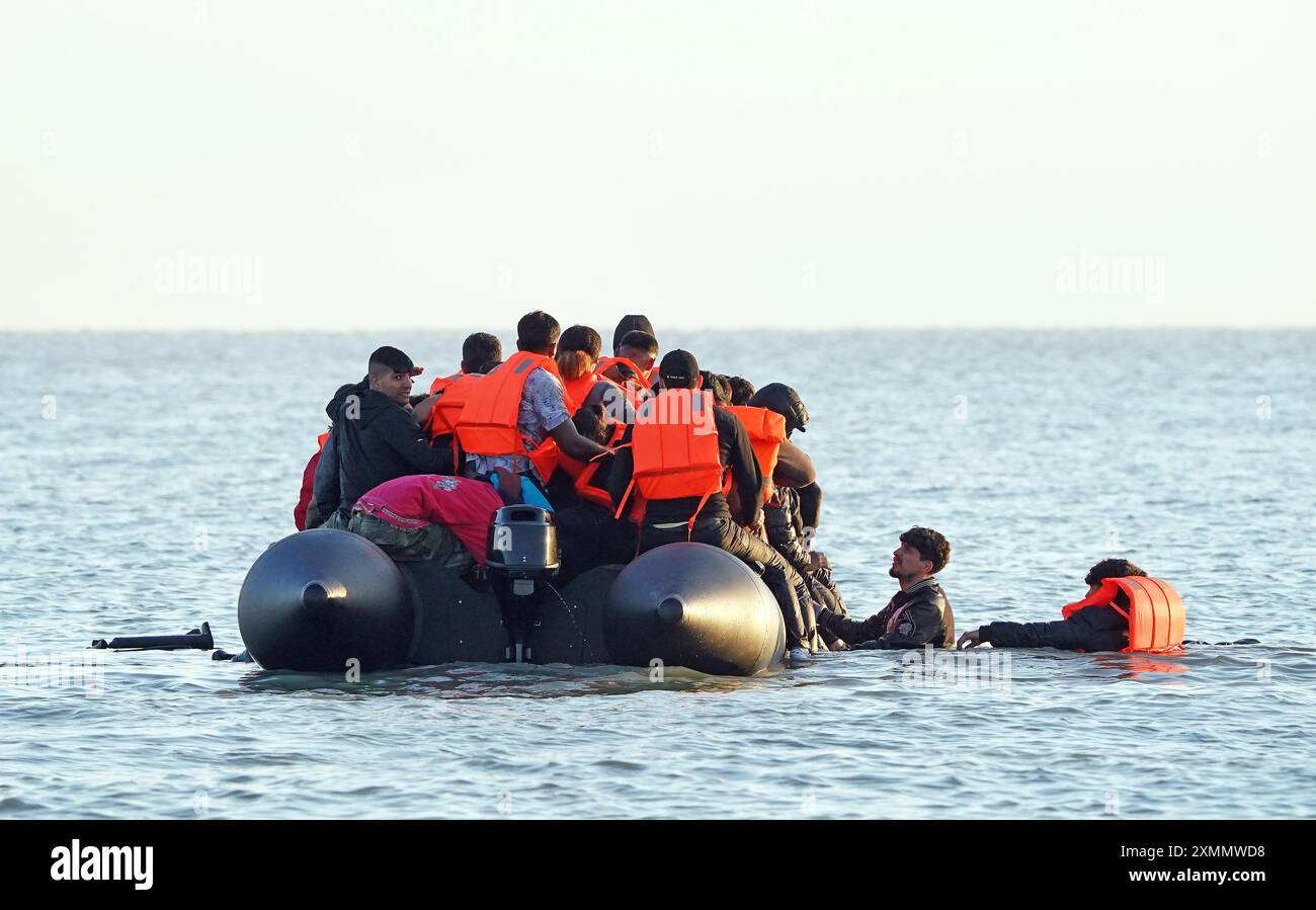 A group of people thought to be migrants wade through the sea to ...