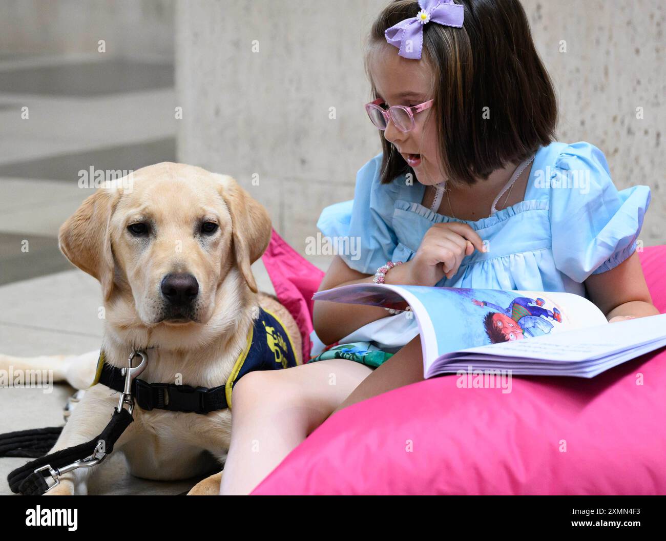 EDITORIAL USE ONLY Kathryn, aged six, reads to Labrador puppy Ron at a ...