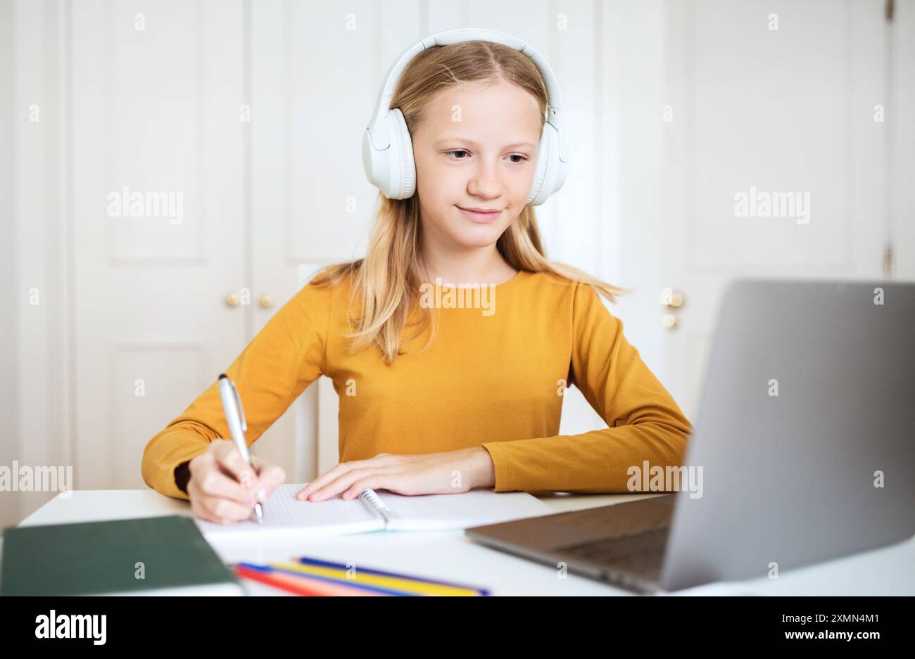 Teen Girl Taking Notes While Using a Laptop and Headphones Stock Photo ...