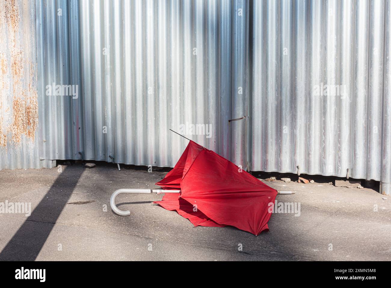Broken red umbrella on the ground in a city street, with a shuttered ...