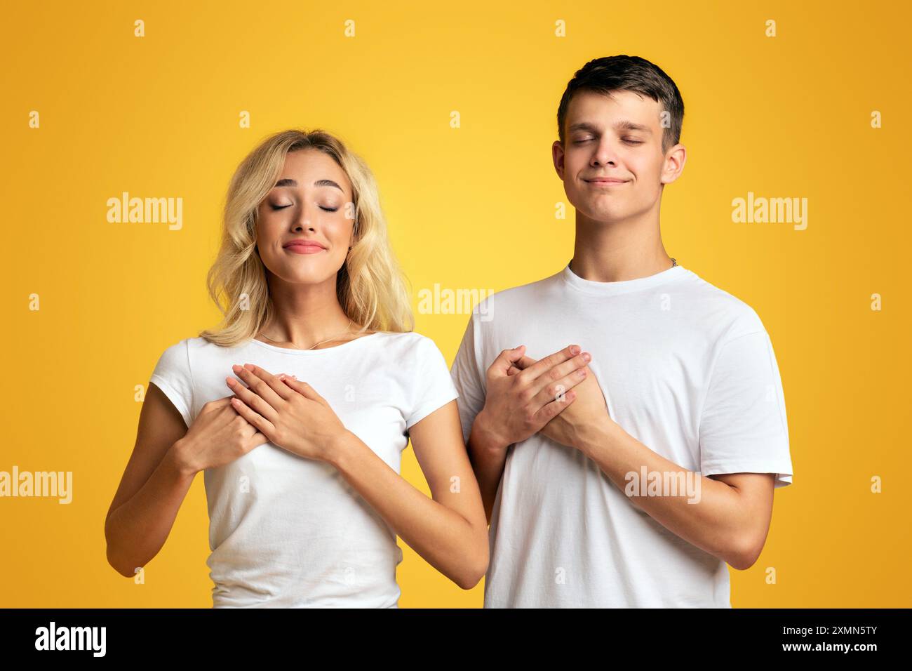 Grateful young couple keeping both palms on chest, expressing ...