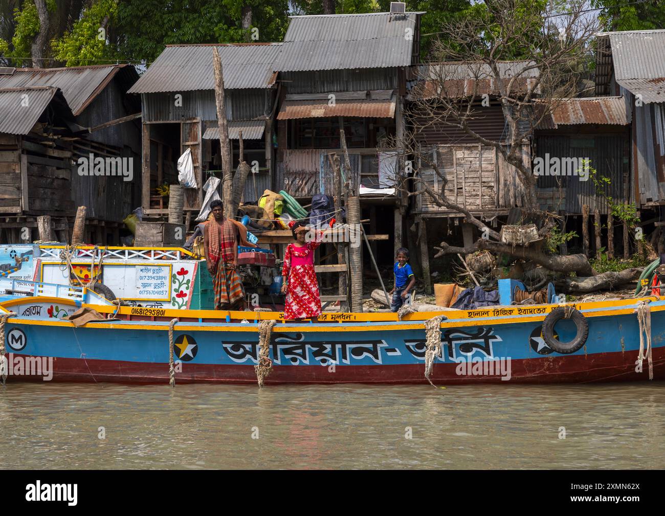 Bangladeshi family on a boat anchored in front of houses in Sundarbans ...