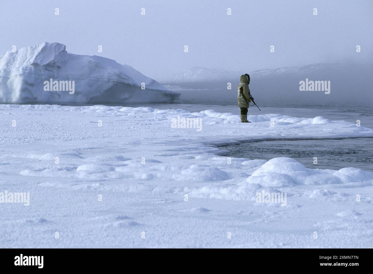 A hooded person holding a rifle and standing amidst snow, Nunavut ...