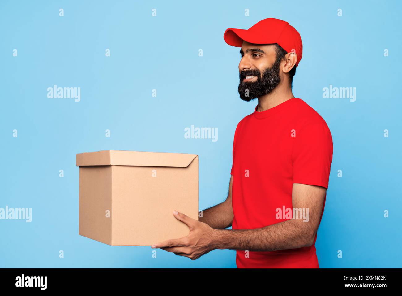 Smiling Delivery Man Holding Cardboard Box Against Blue Background ...