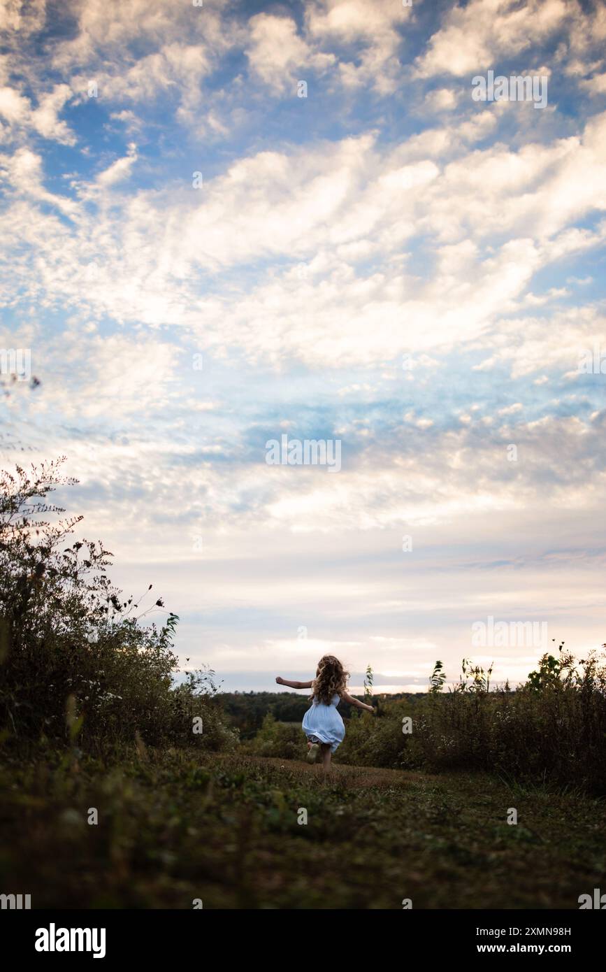 Back view of little girl running through field blue skies Stock Photo ...