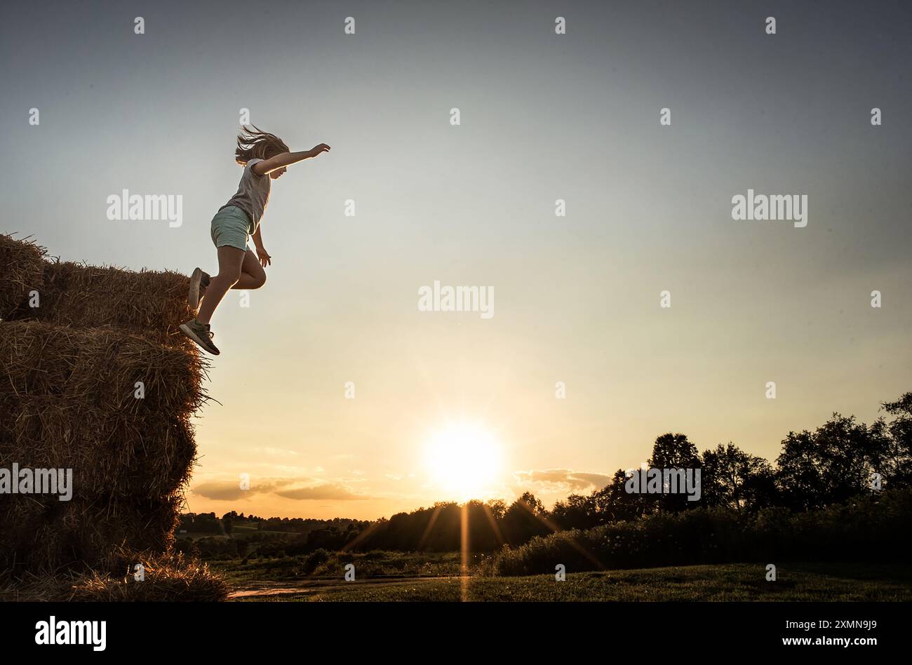 Young girl jumping from straw bales at sunset Stock Photo - Alamy