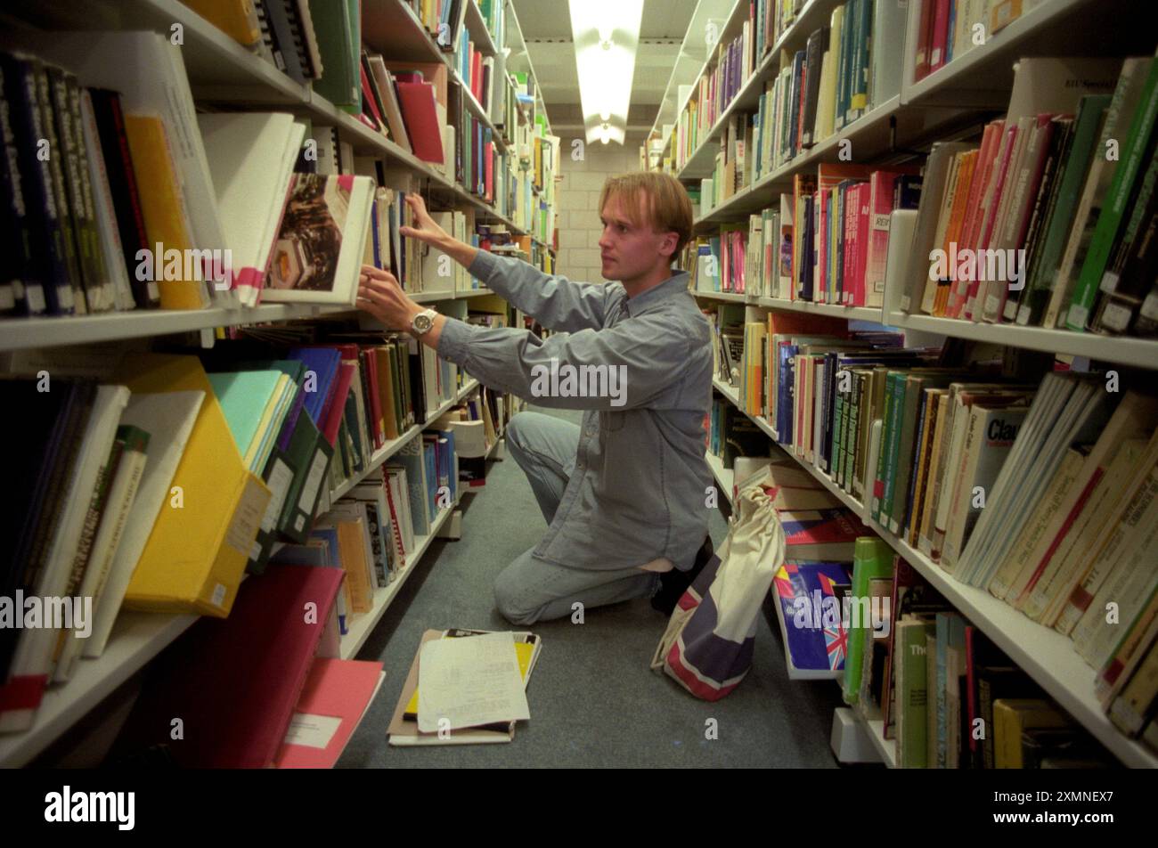 An undergraduate searches through rows of reference books in a library ...
