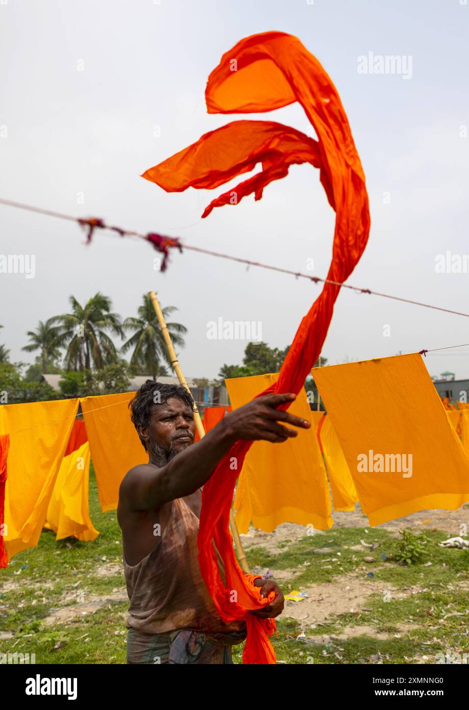 Bangladeshi worker hanging orange fabrics under the sun, Dhaka Division ...