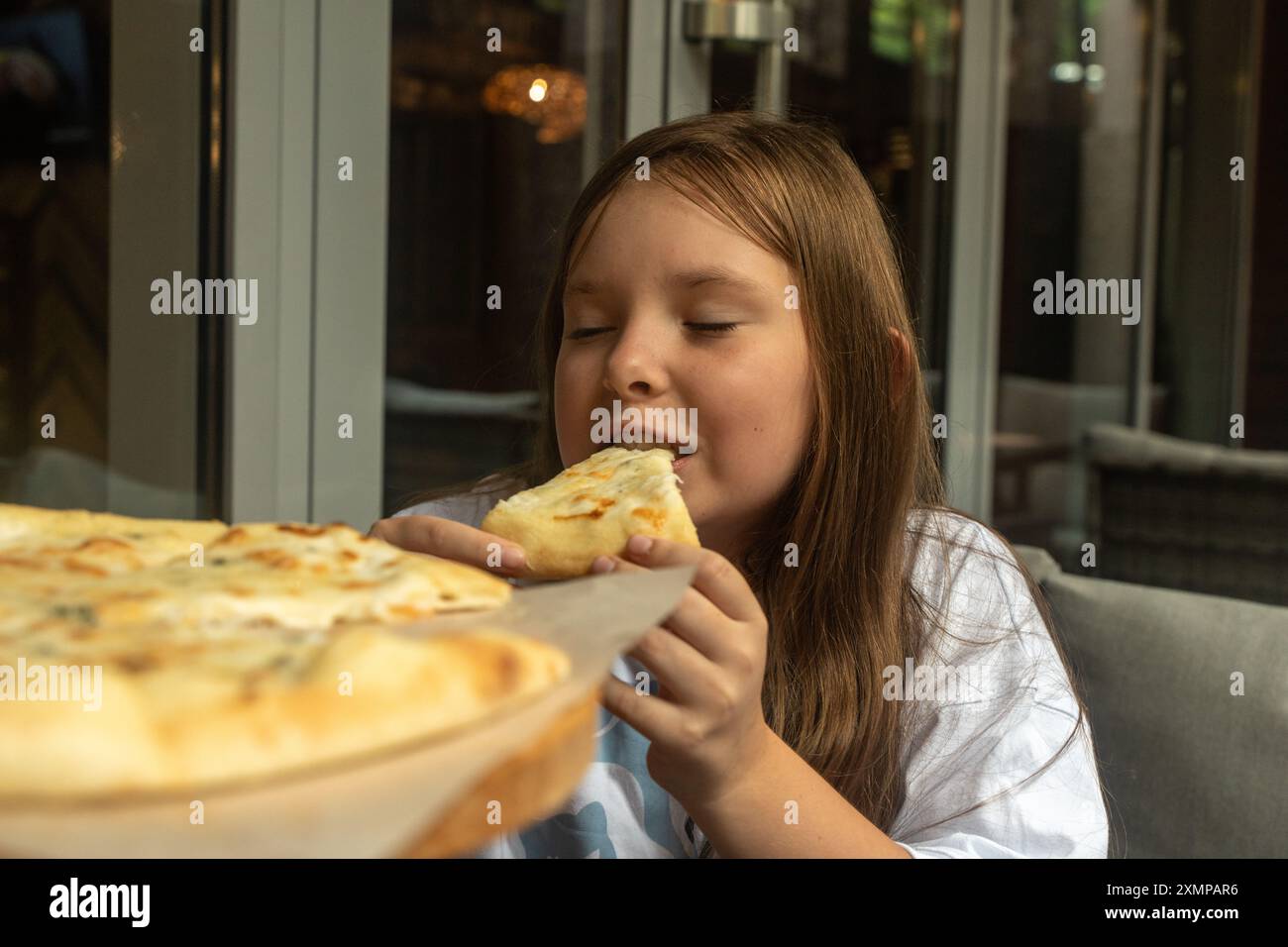 Little pre-teen girl eating cheese pizza while enjoying the taste with ...