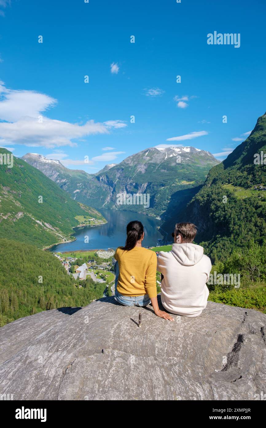 Two people sit on a rock overlooking a picturesque Norwegian fjord ...