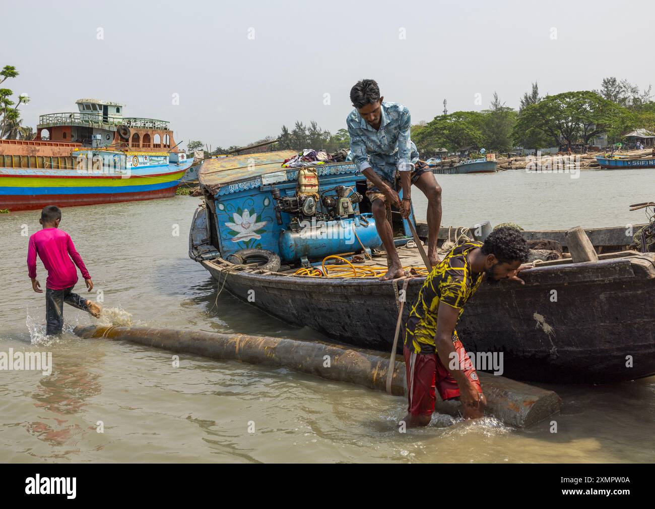 Bangladeshi men attaching a tree trunk to their boat, Barisal Division, Nesarabad, Bangladesh ...