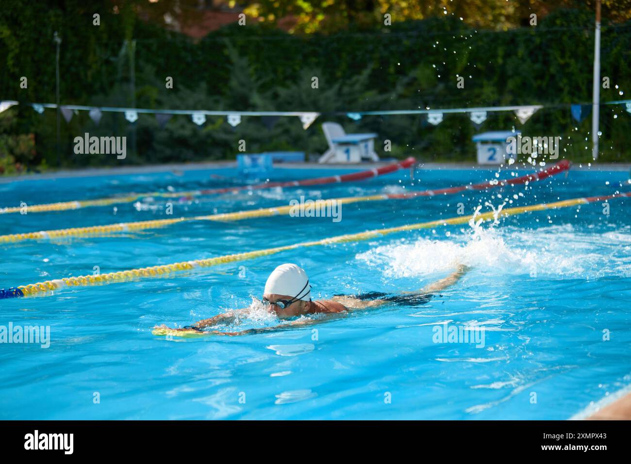 Athletic man, swimmer in white swim cap and goggles swims laps in pool ...