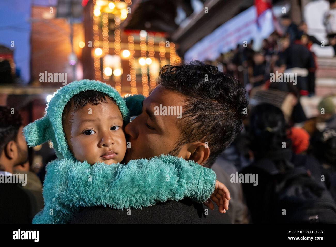 Young child cuddles in father's arms during evening Diwali festival of ...