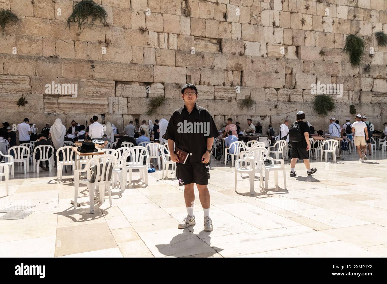 A Chinese tourist poses for a photo while Jewish worshippers pray at ...