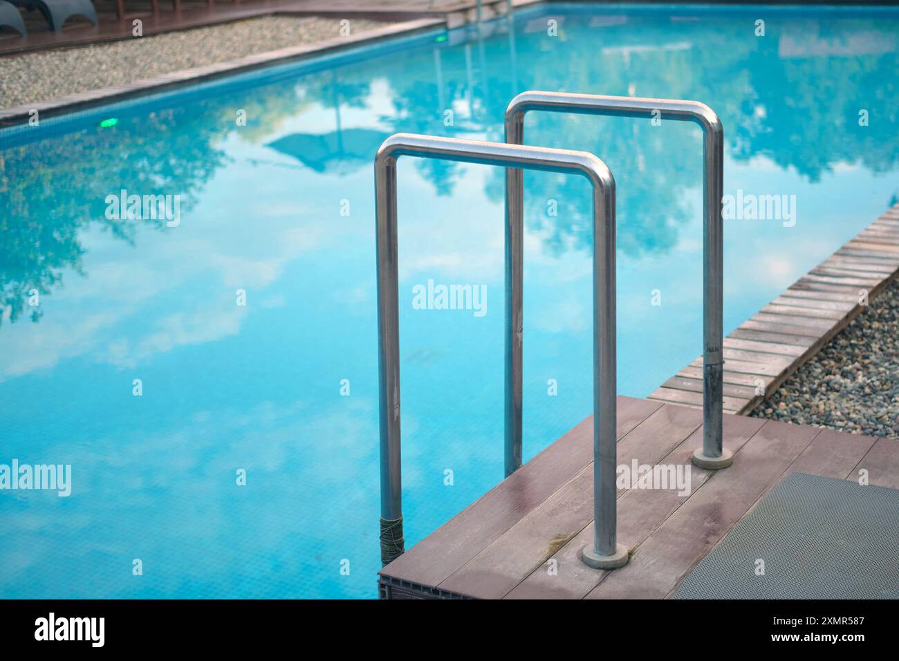 Metal pool ladder leading into a clear blue swimming pool with wooden ...