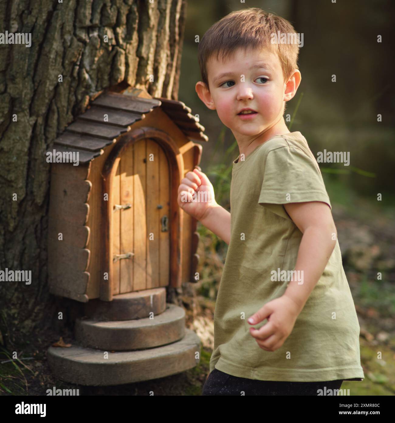 Child knocking on a small fairy door in a tree trunk while looking back ...